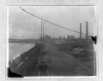 View of tracks by the waterfront with smoke stacks in the background to ...